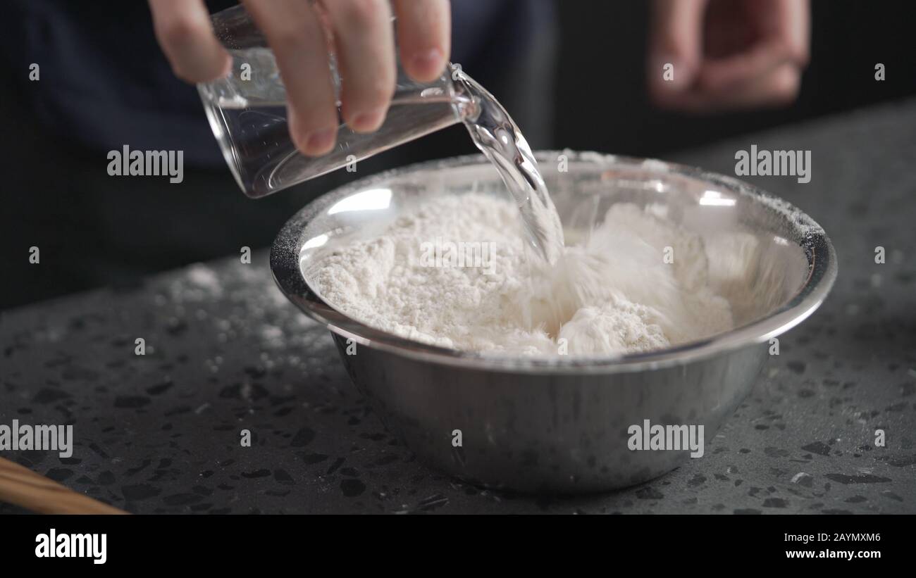 man adds wet ingredients into flour in steel bowl on concrete ...