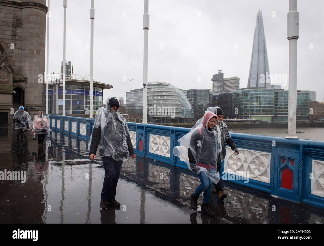 People cross Tower Bridge, in London, during a heavy downpour of rain ...