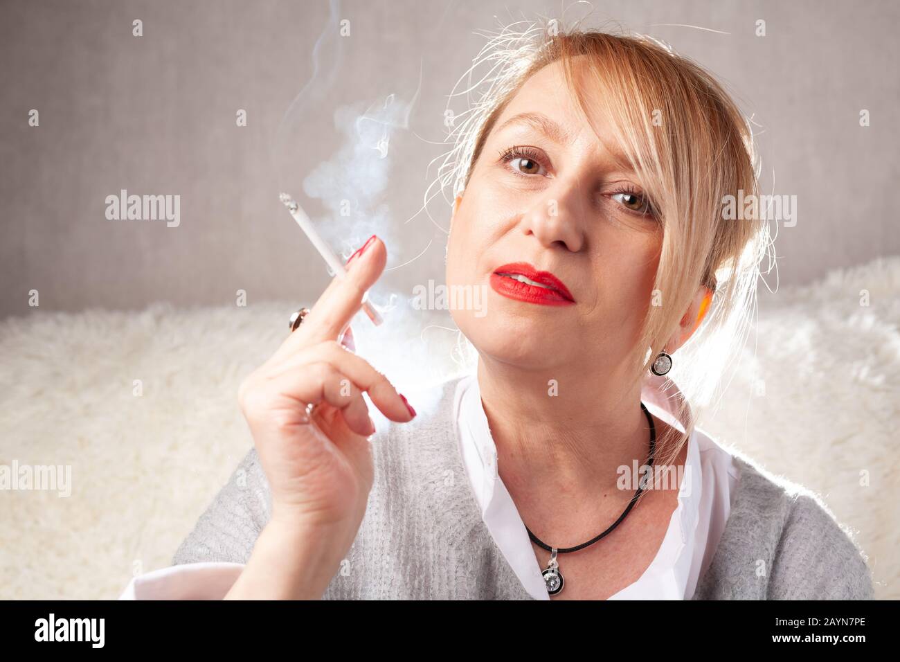 A middle-aged woman smokes in the living room. Stock photo of a happy ...