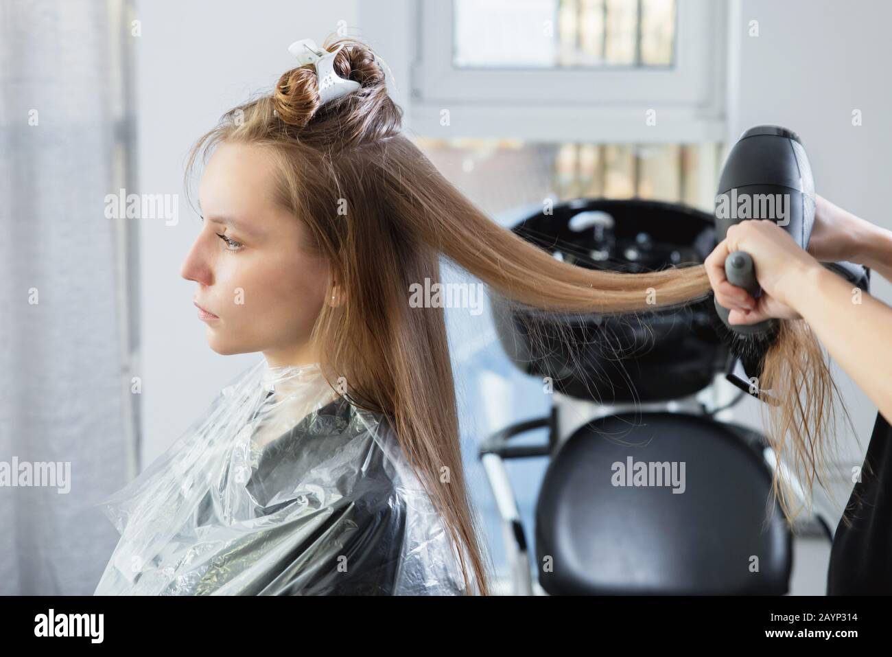 Close up of hairdressers hands drying long blond hair with blow dryer ...