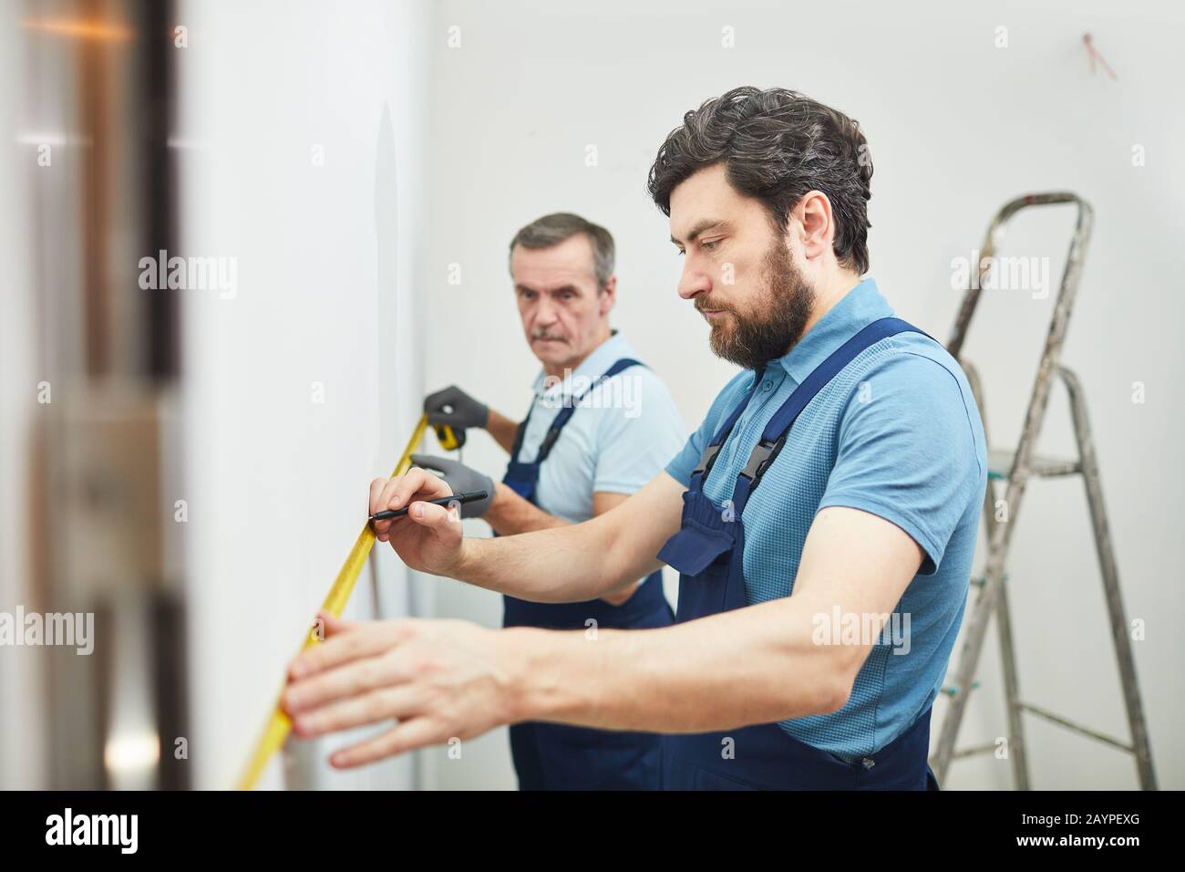 Side view portrait of two construction workers measuring wall while ...