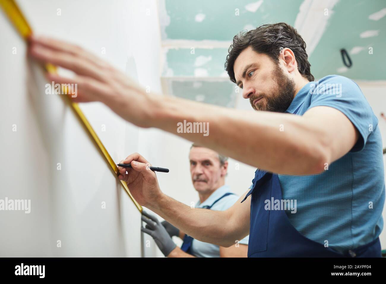 Low angle portrait of two construction workers measuring wall while ...