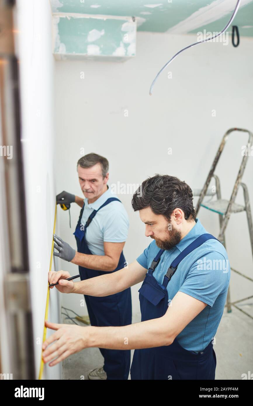High angle portrait of two construction workers measuring wall while ...