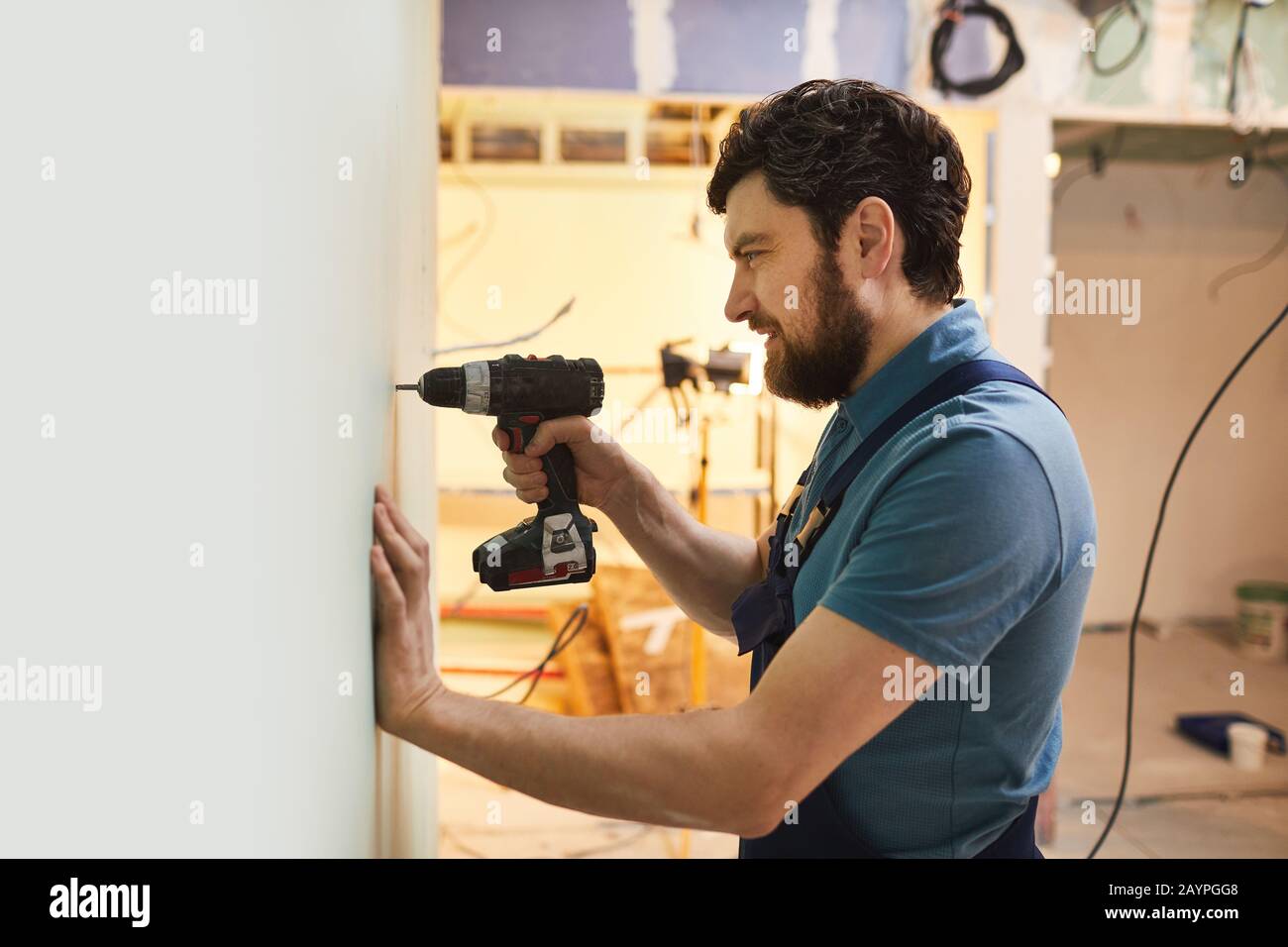 Side view portrait of bearded construction worker drilling wall while ...