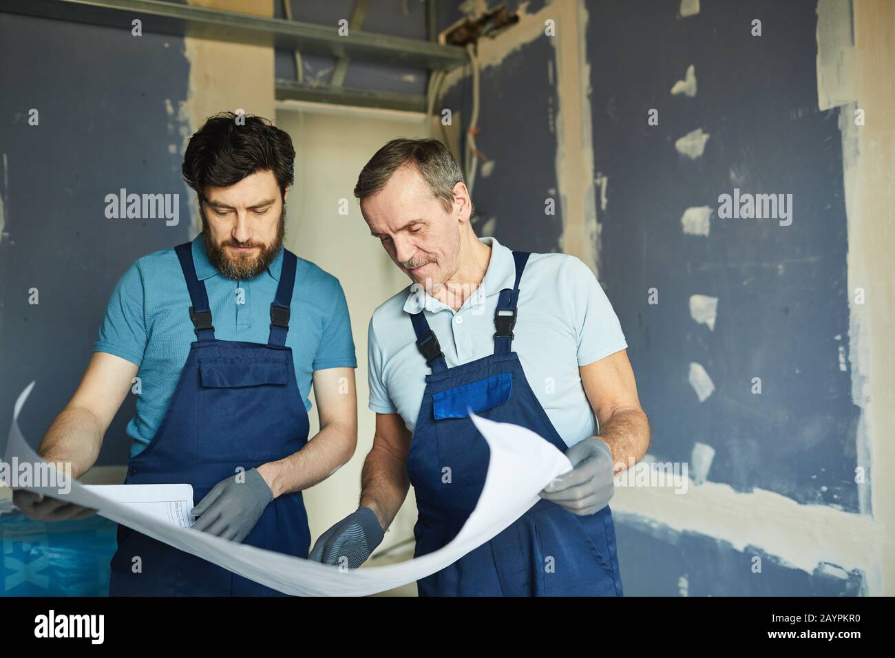 Waist up portrait of two construction workers holding plans and ...