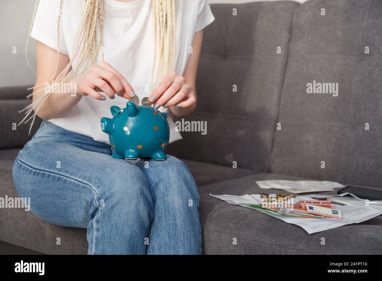 Young woman putting coins into money box sitting on sofa at home Stock ...