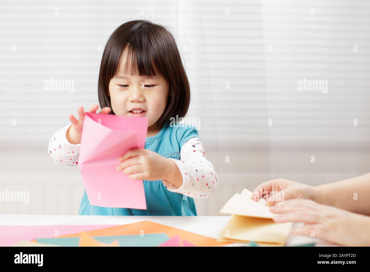 toddler girl learn making Origami at home against white background ...