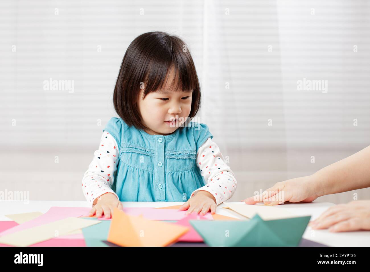 toddler girl learn making Origami at home against white background ...