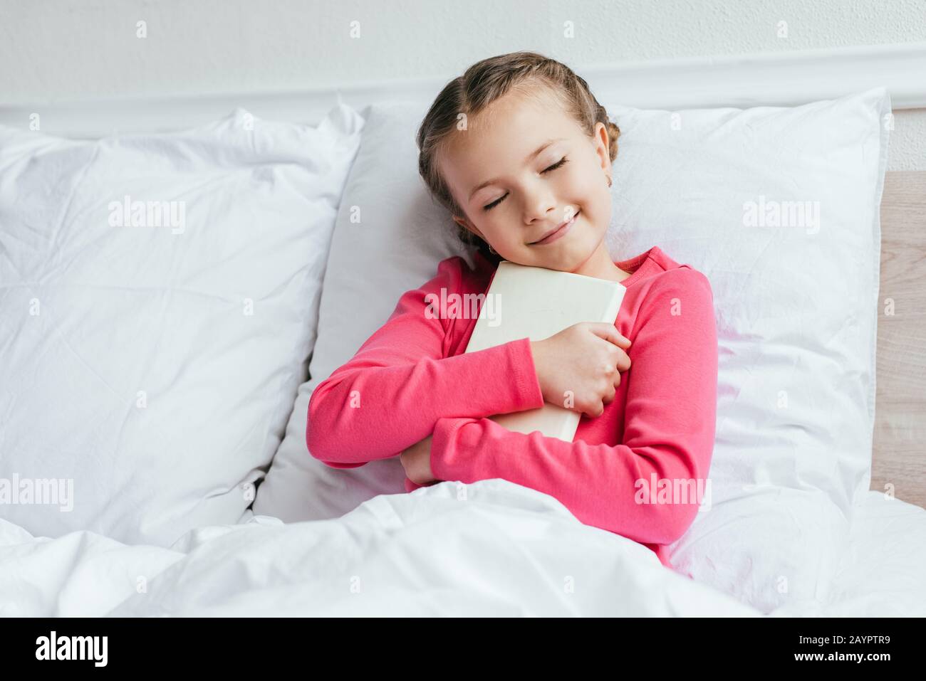 cheerful adorable kid hugging book while sitting on bed Stock Photo - Alamy