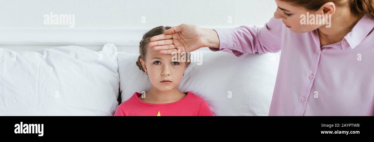 panoramic shot of mother touching forehead of ill daughter with fever ...