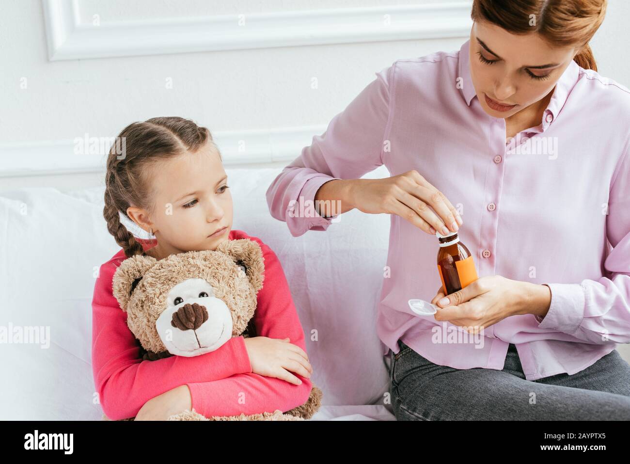 mom giving syrup to sick daughter with teddy bear Stock Photo - Alamy
