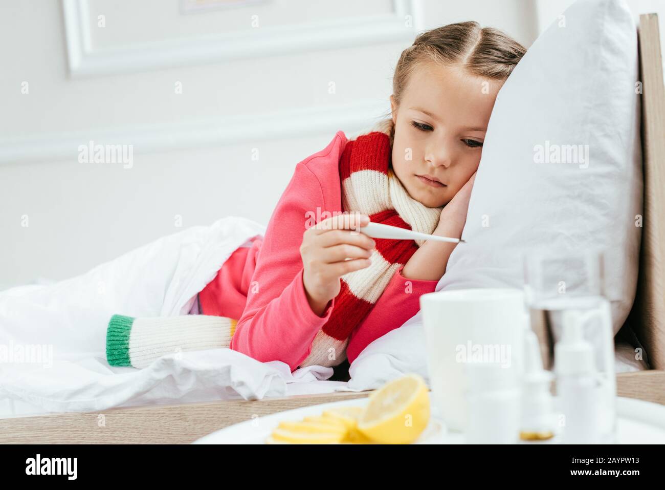 sick upset child with fever in scarf looking on thermometer while lying ...