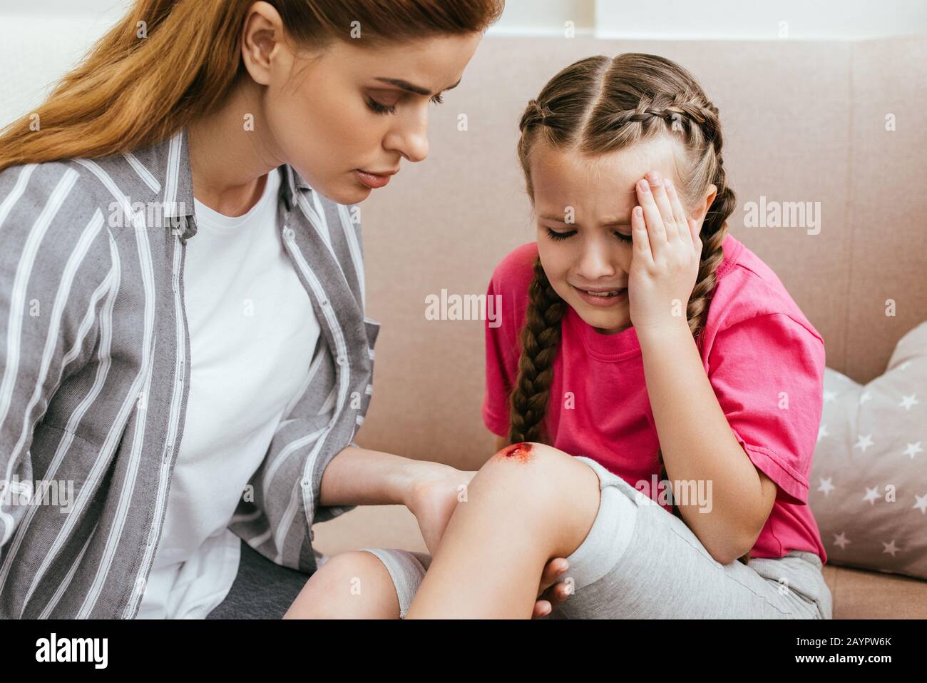 mother holding leg with wound on knee while emotional daughter crying ...