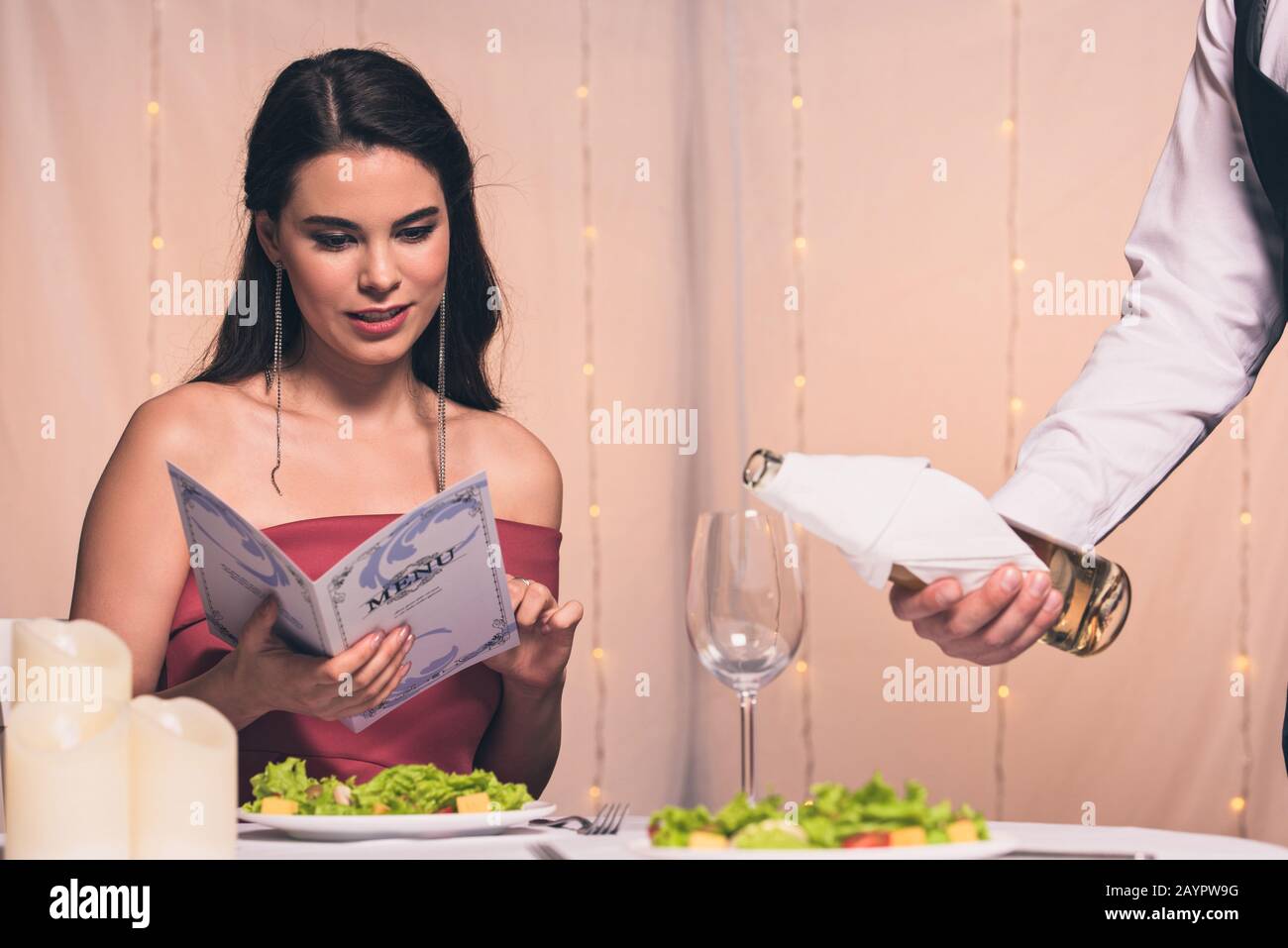 attractive, elegant girl reading menu while waiter pouring white wine ...
