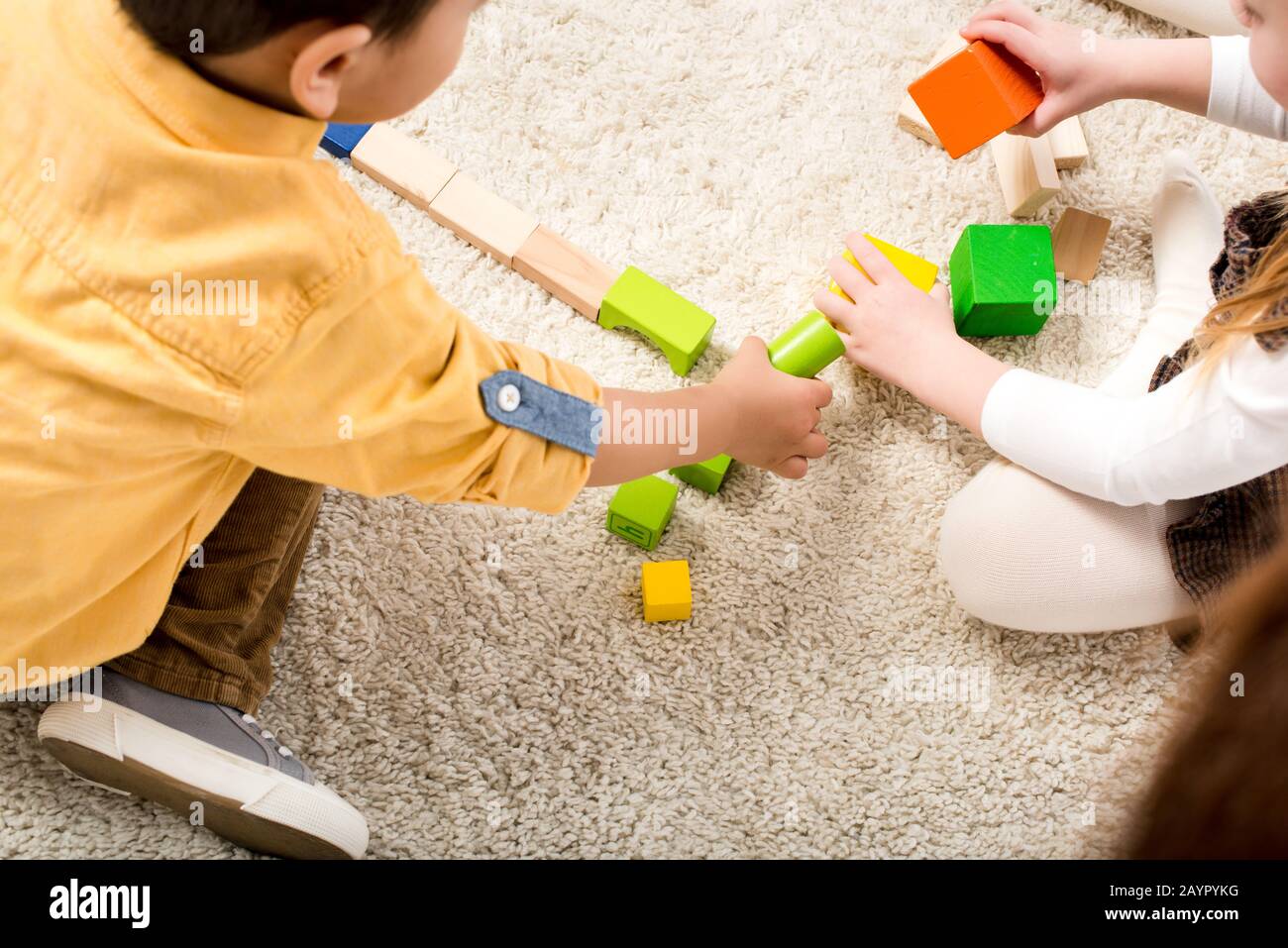 cropped view of kids playing with colorful wooden blocks on carpet ...