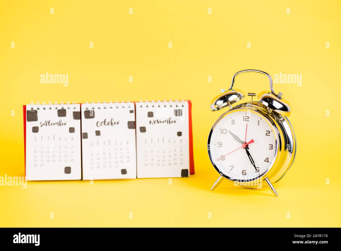Alarm clock and calendar with autumnal months on yellow background ...
