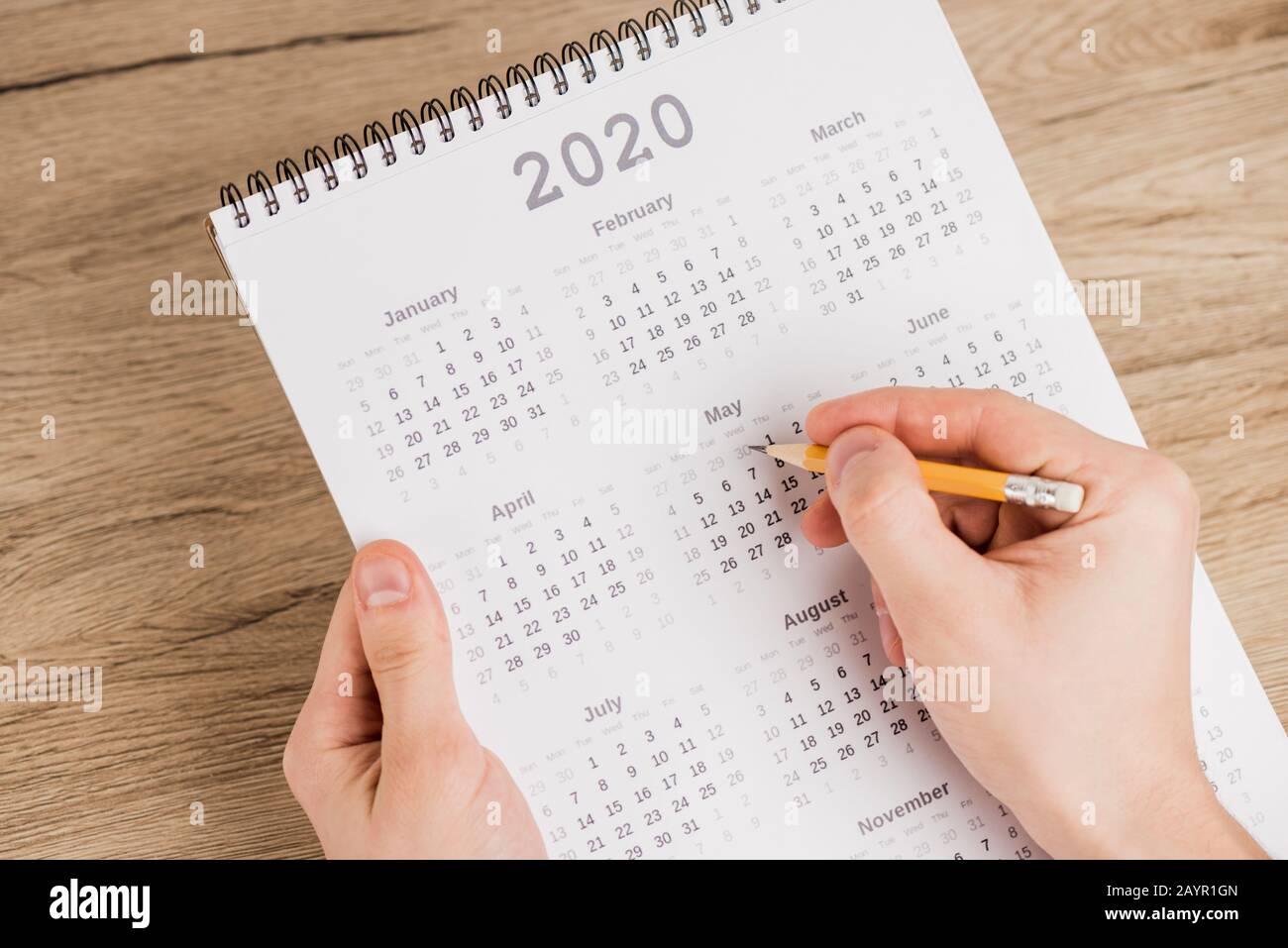 Cropped view of man noting date with pencil on calendar on wooden ...