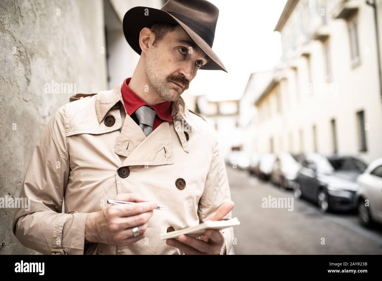 Detective writing on a notebook while standing against an old wall ...