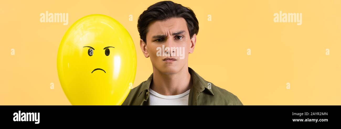 panoramic shot of skeptical man holding angry balloon, isolated on ...