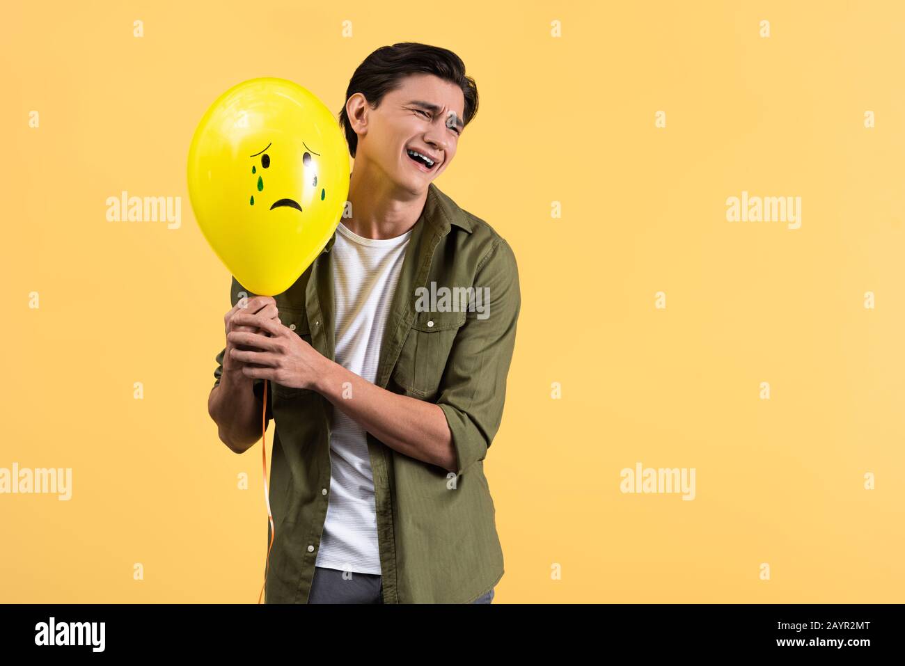 sad crying young man holding balloon with tears, isolated on yellow ...