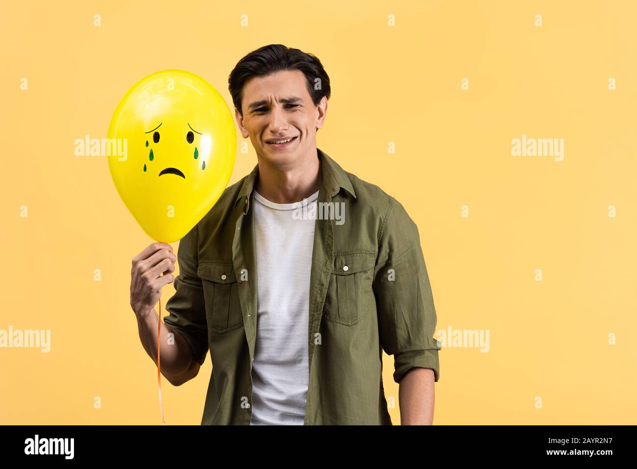 sad young man holding crying balloon with tears, isolated on yellow ...