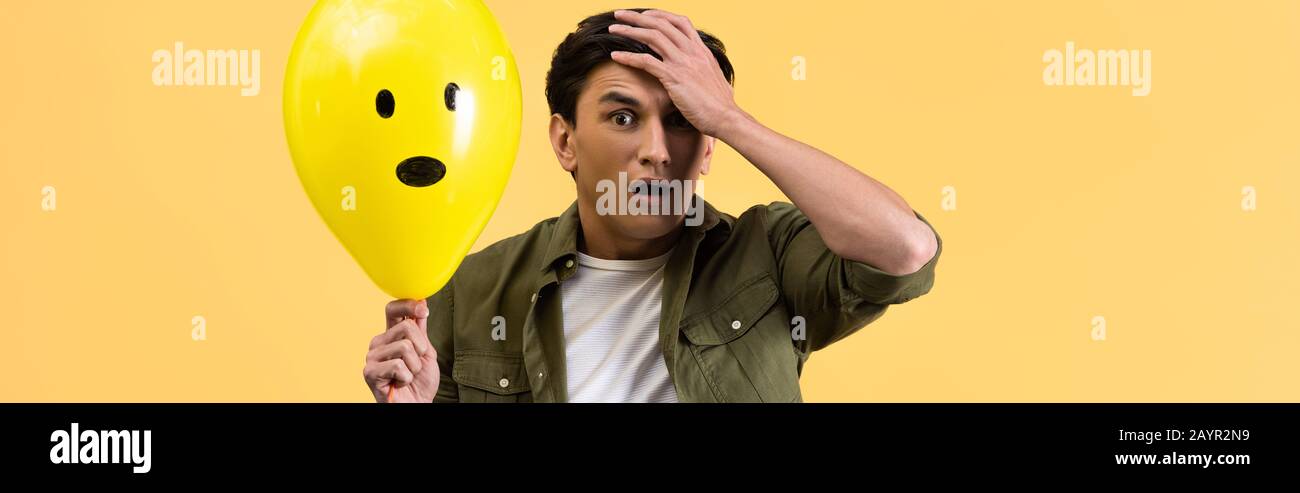 panoramic shot of worried man holding shocked balloon, isolated on ...