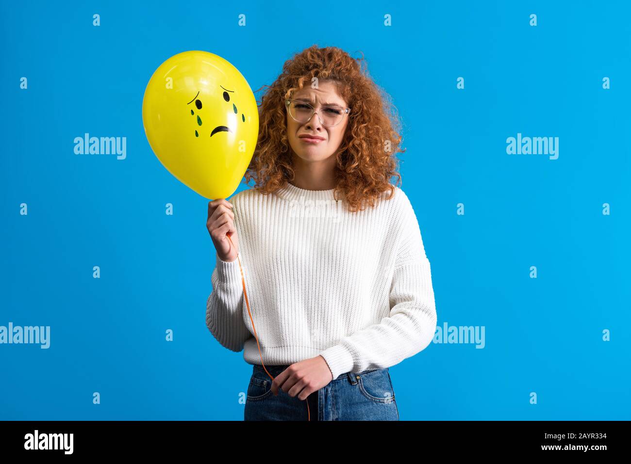 upset girl holding yellow balloon with crying face, isolated on blue ...