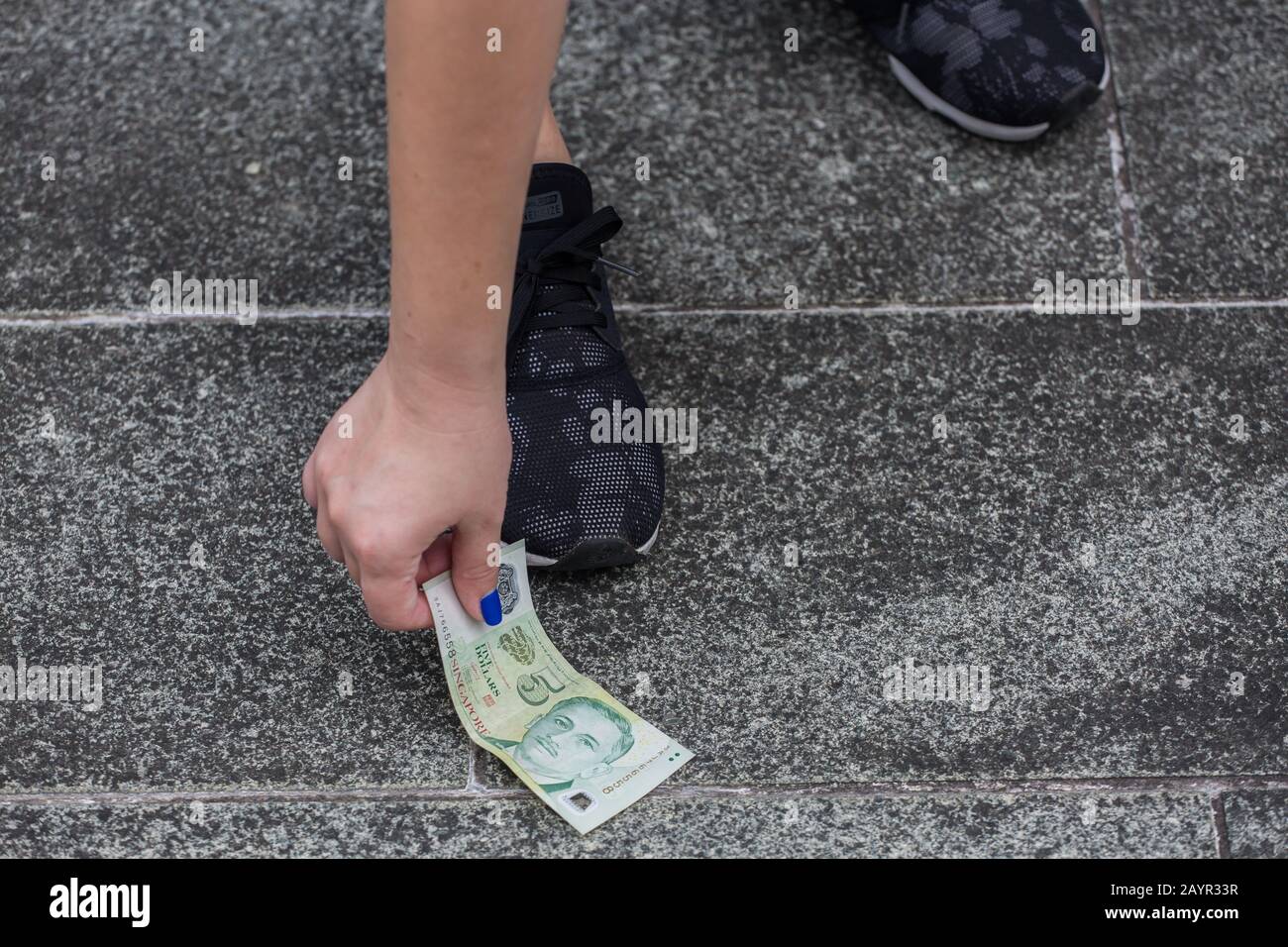 Bend down to pick up a piece of Singapore five dollar green colour note ...