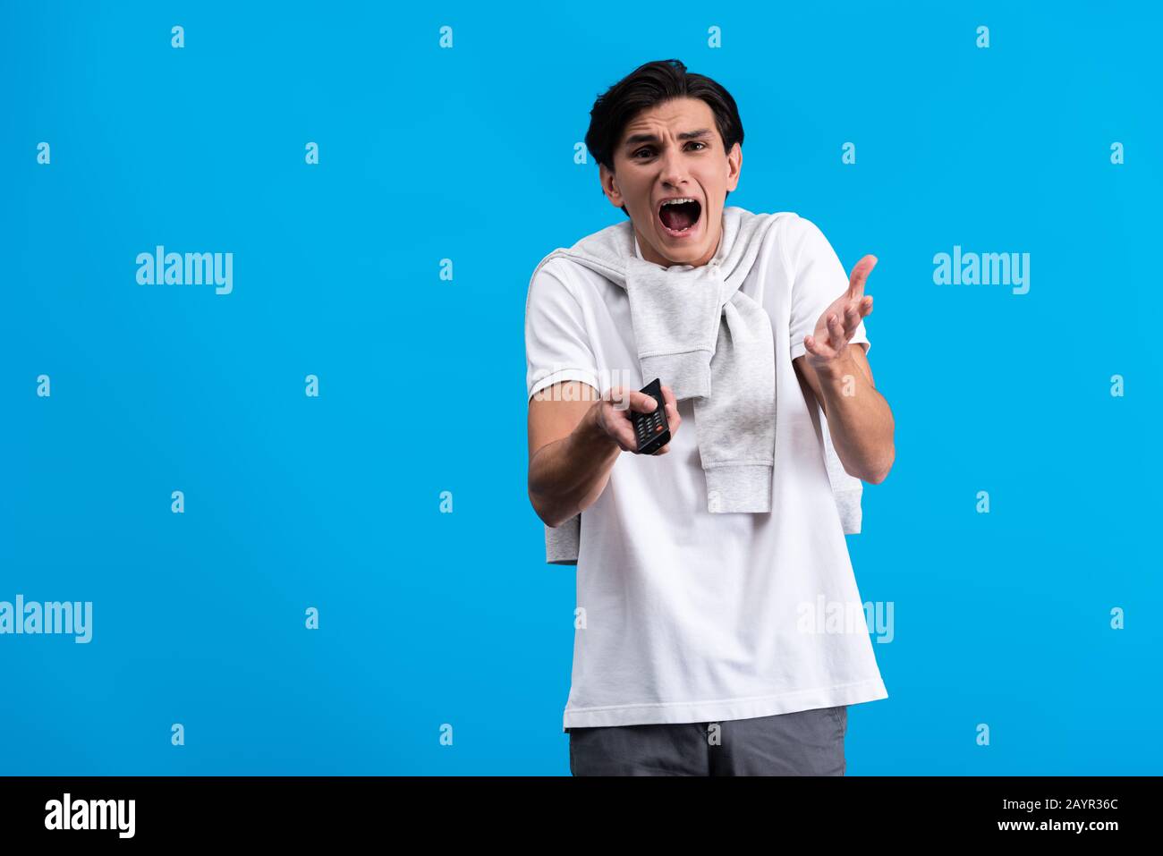 angry yelling man watching tv with remote controller, isolated on blue ...