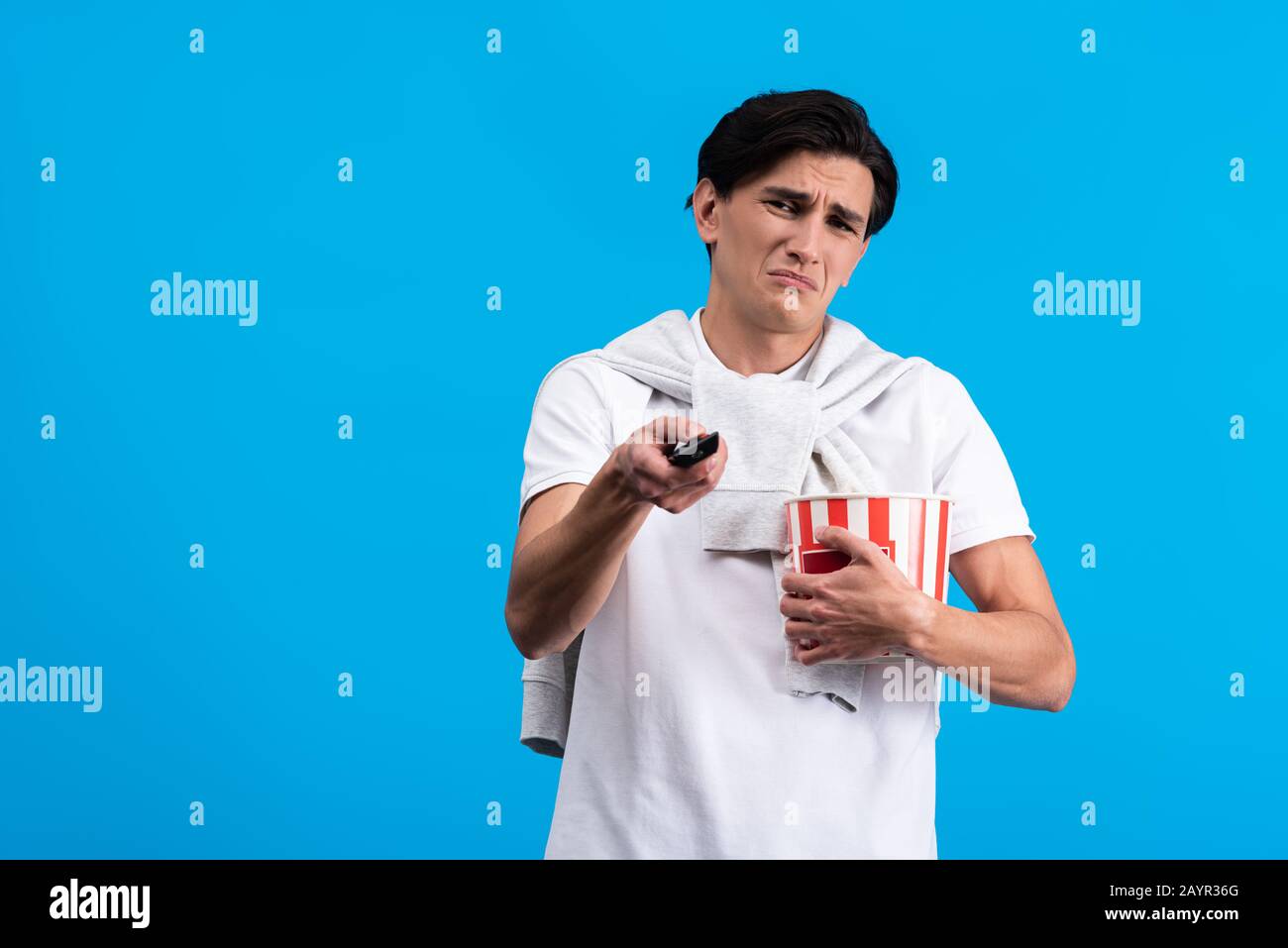 sad young man watching tv with remote controller and popcorn, isolated ...
