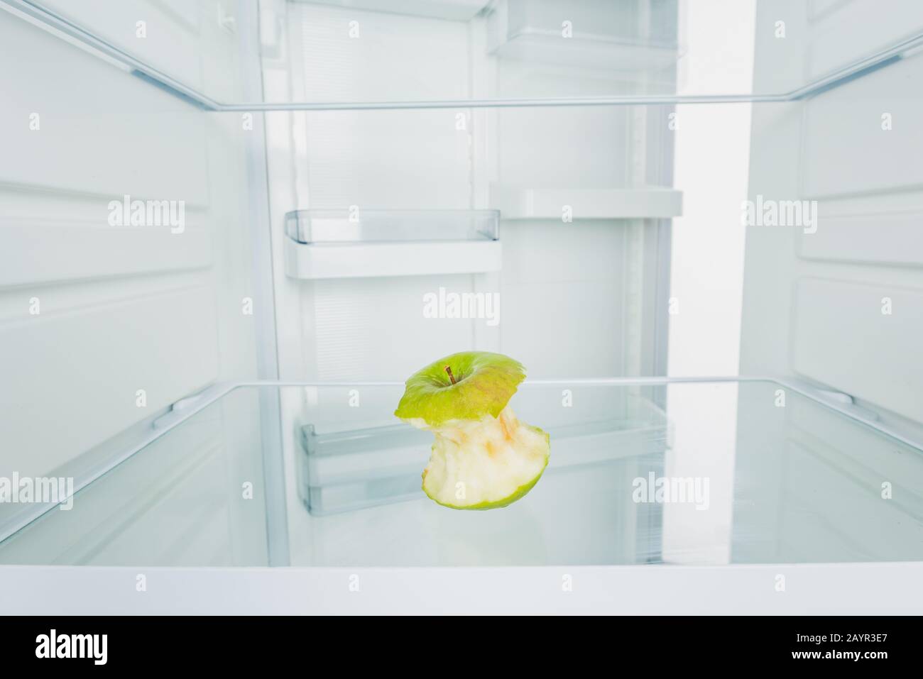 Gnawed green apple on shelf of refrigerator with open door isolated on ...