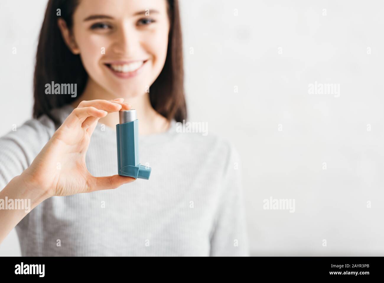 Selective focus of girl holding inhaler and smiling at camera on white ...