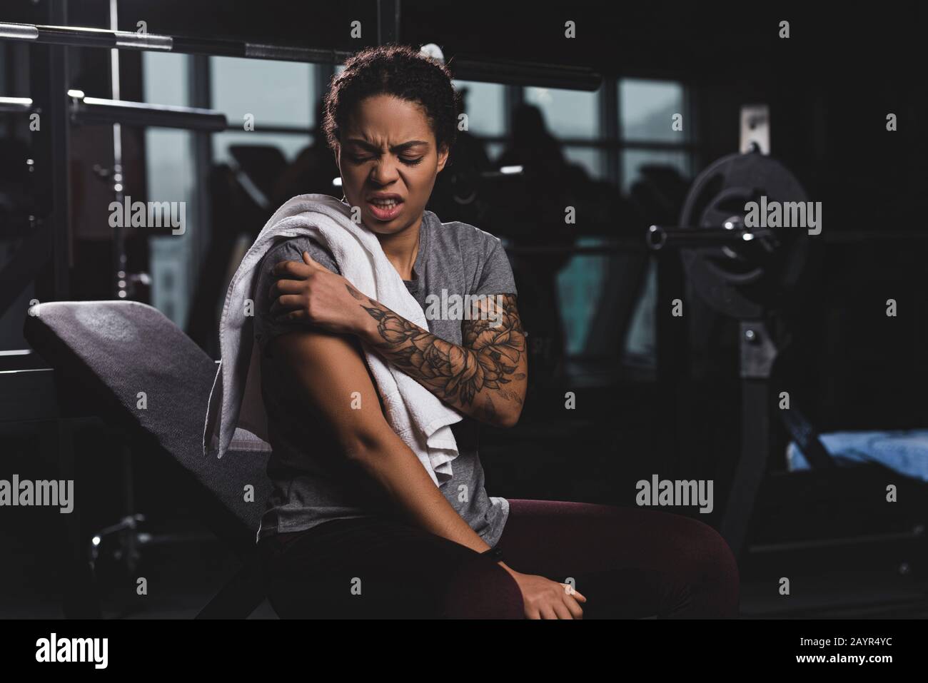 injured african american woman with tattoo touching hand while ...