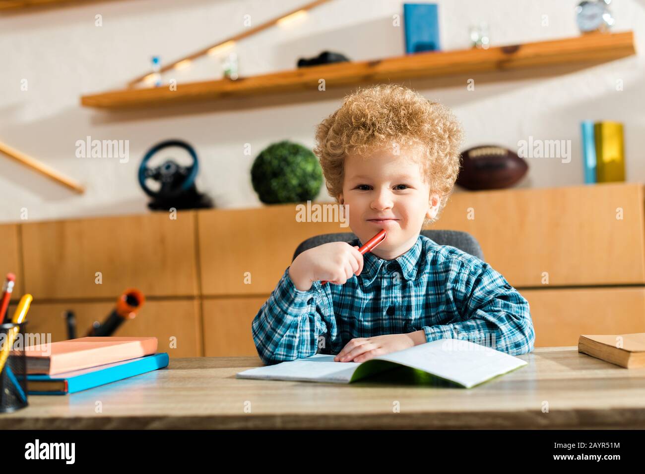 happy and curly kid holding pen near notebook and books on desk Stock ...