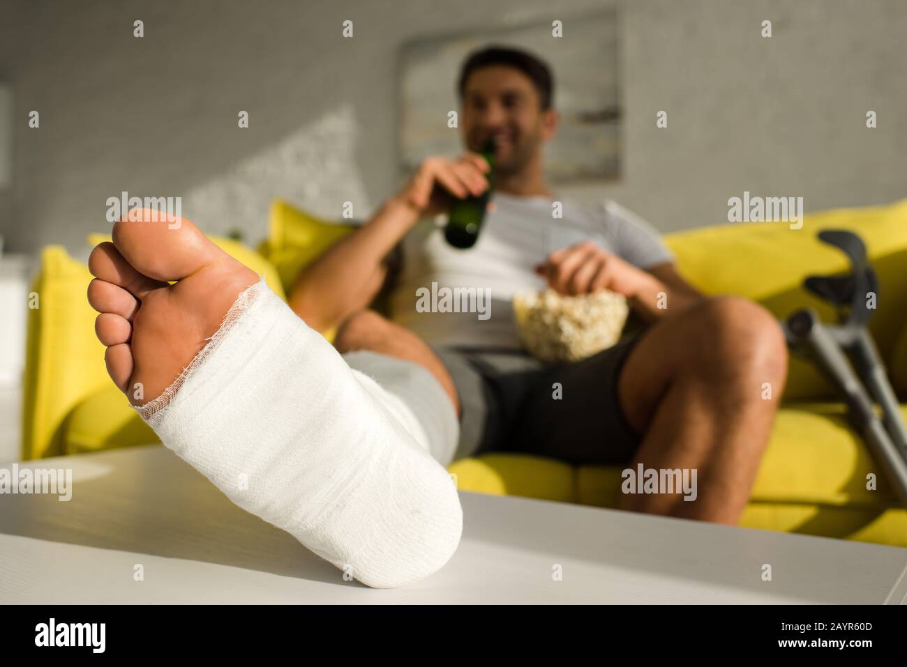 Selective focus of man with broken leg drinking beer and eating popcorn ...