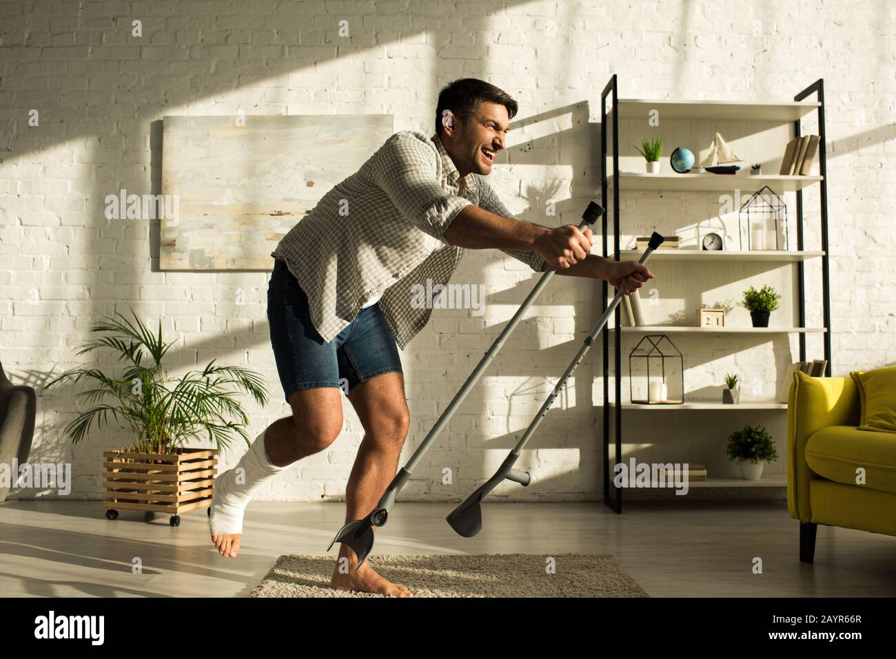 Side view of cheerful man with broken leg holding crutches while ...