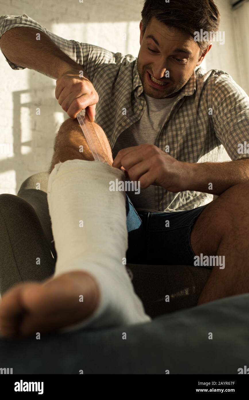 Selective focus of exited man scratching with ruler broken leg at home ...