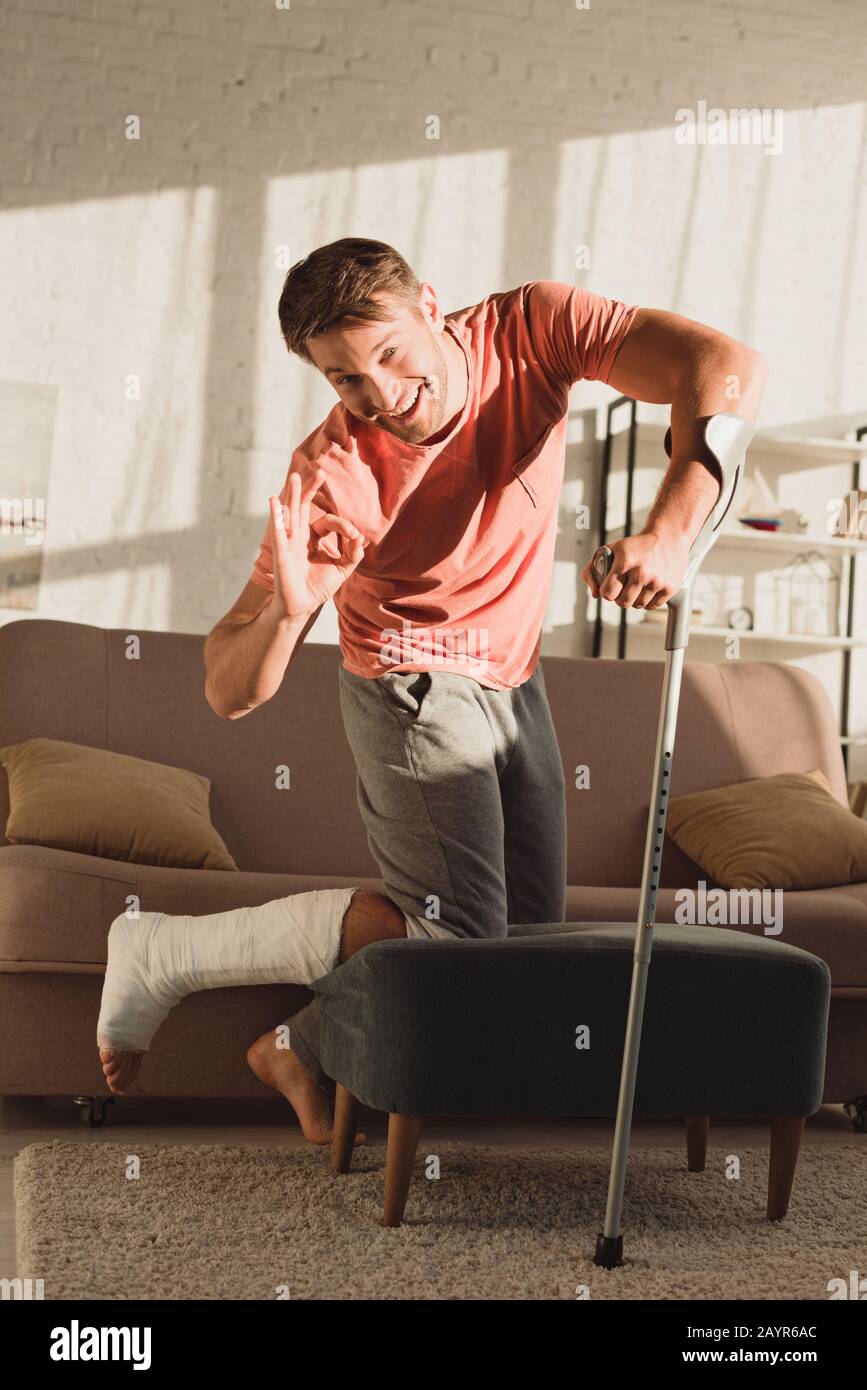 Man with broken leg smiling at camera and showing okay sign at home ...