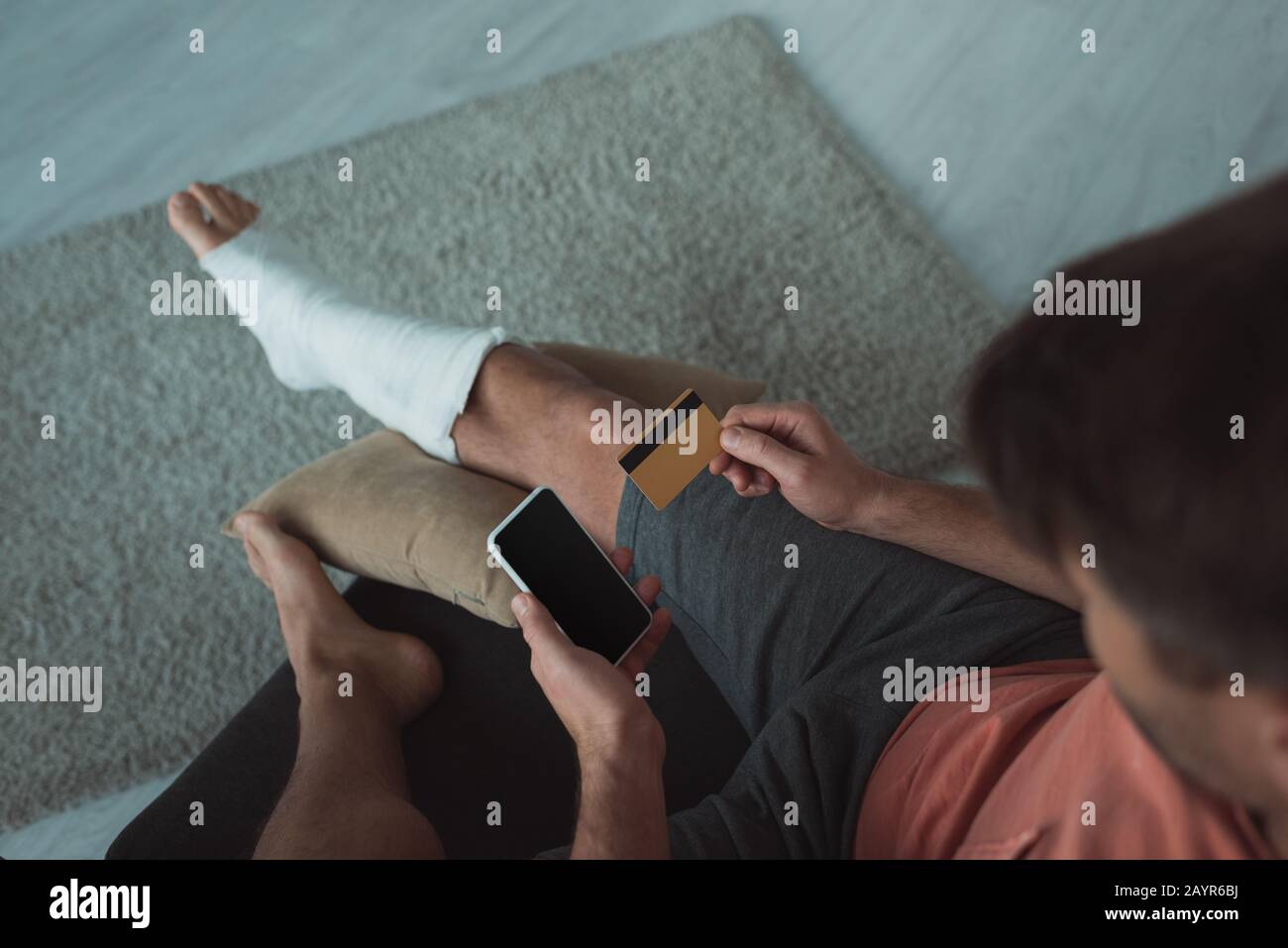 Overhead view of man with broken leg using smartphone and credit card ...
