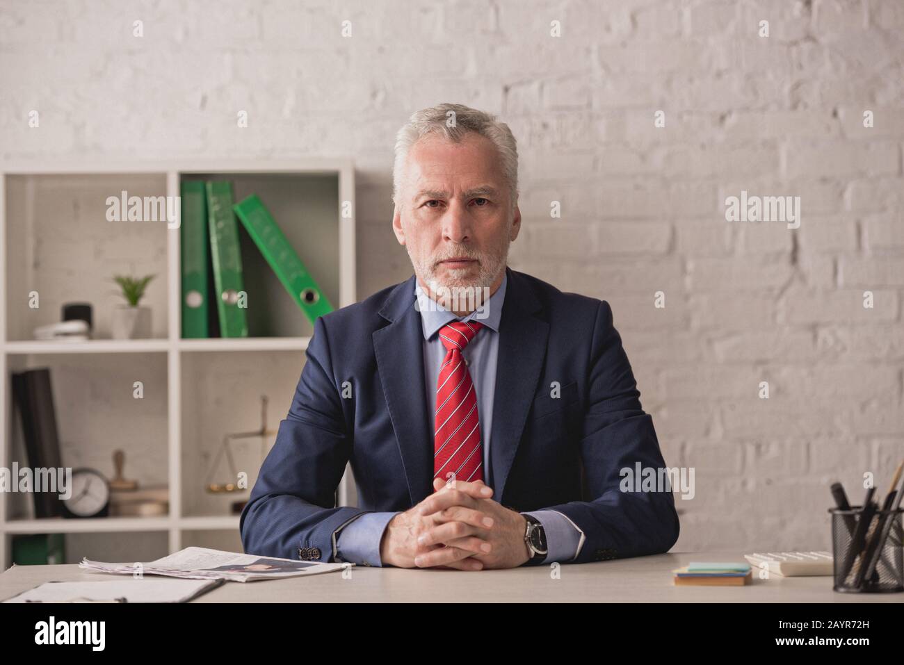 handsome realtor looking at camera while sitting in clenched hands ...