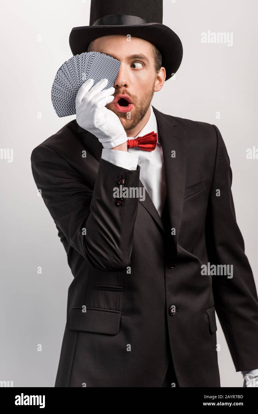 shocked magician with open mouth holding playing cards, isolated on ...