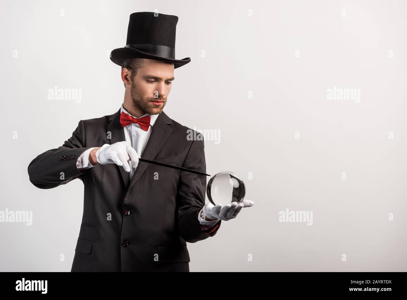 professional magician holding wand and magic ball, isolated on grey ...