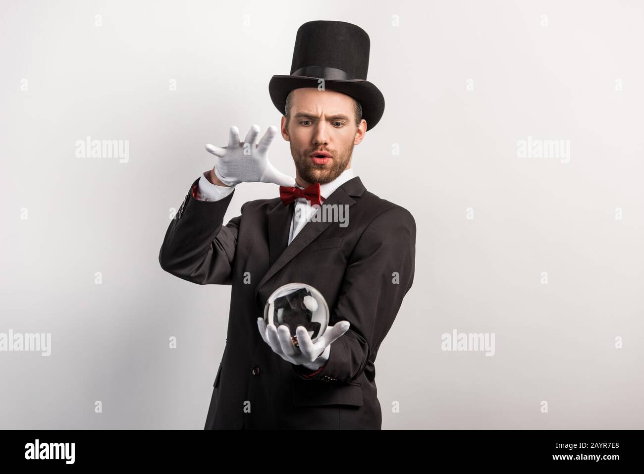 focused professional magician holding magic ball, isolated on grey ...