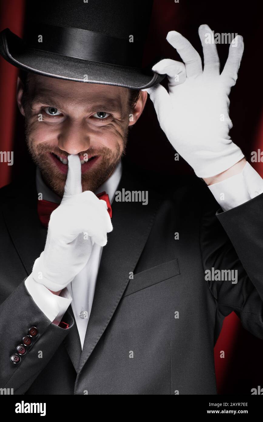 scary smiling magician winking and showing silence symbol in circus ...