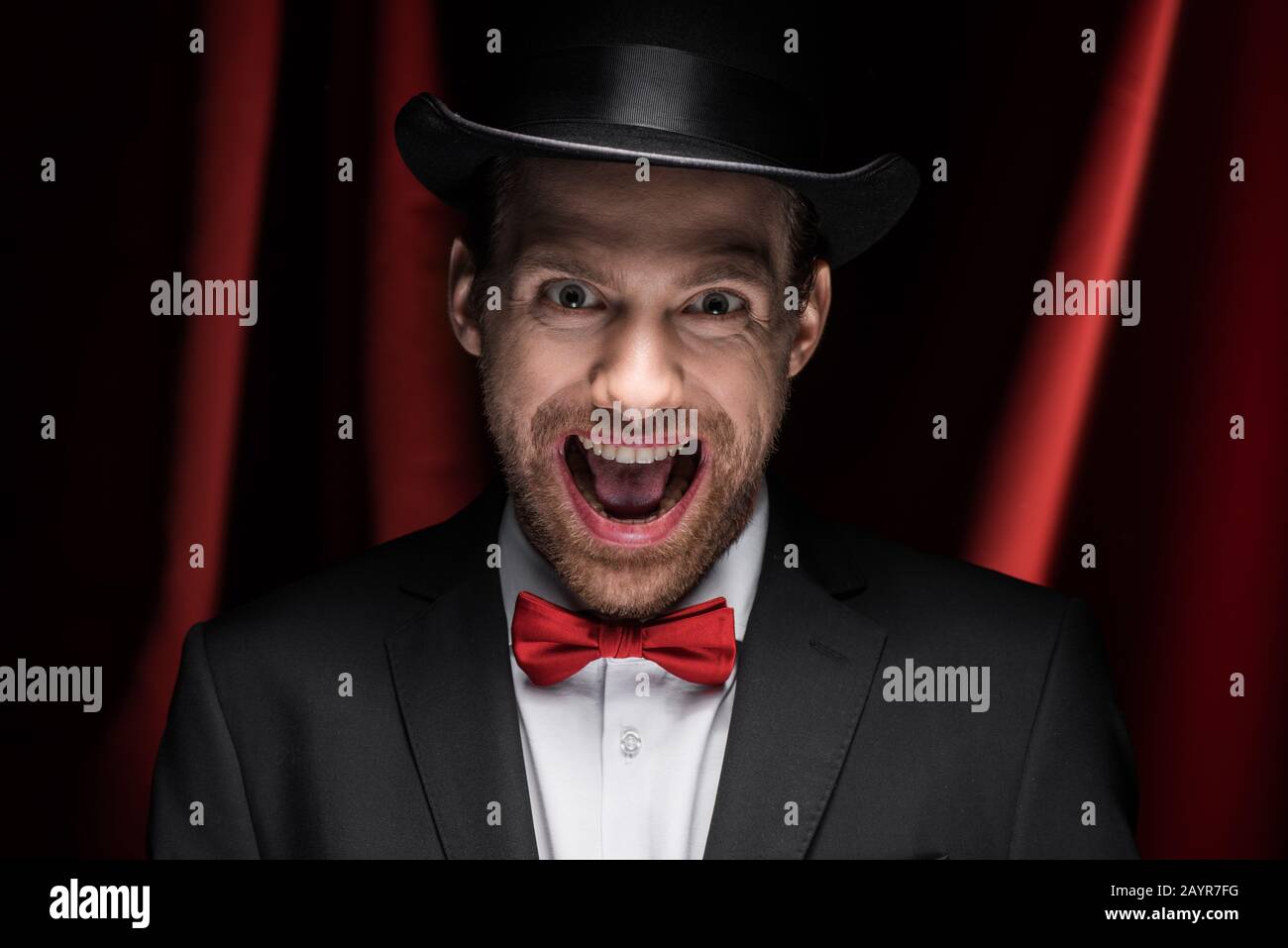 scary excited magician with open mouth in circus with red curtains ...