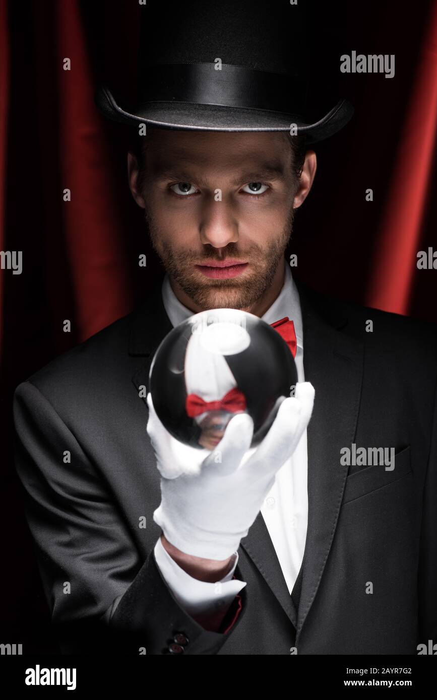 professional magician holding magic ball in circus with red curtains ...