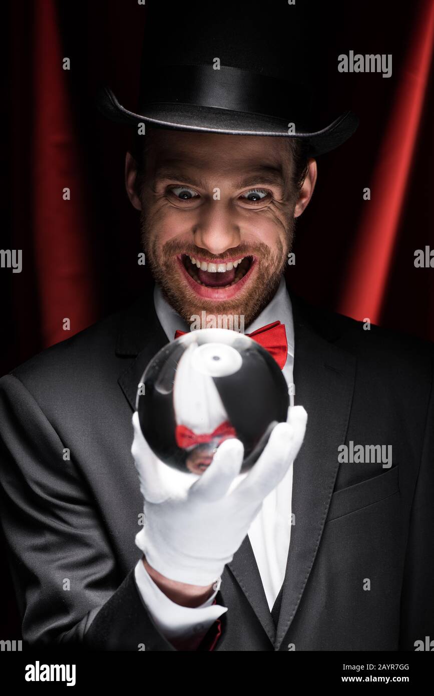 excited scary magician looking at magic ball in circus with red ...
