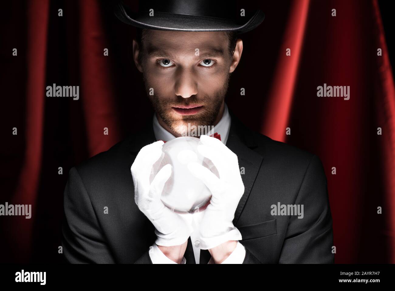 professional magician holding magic ball in circus with red curtains ...