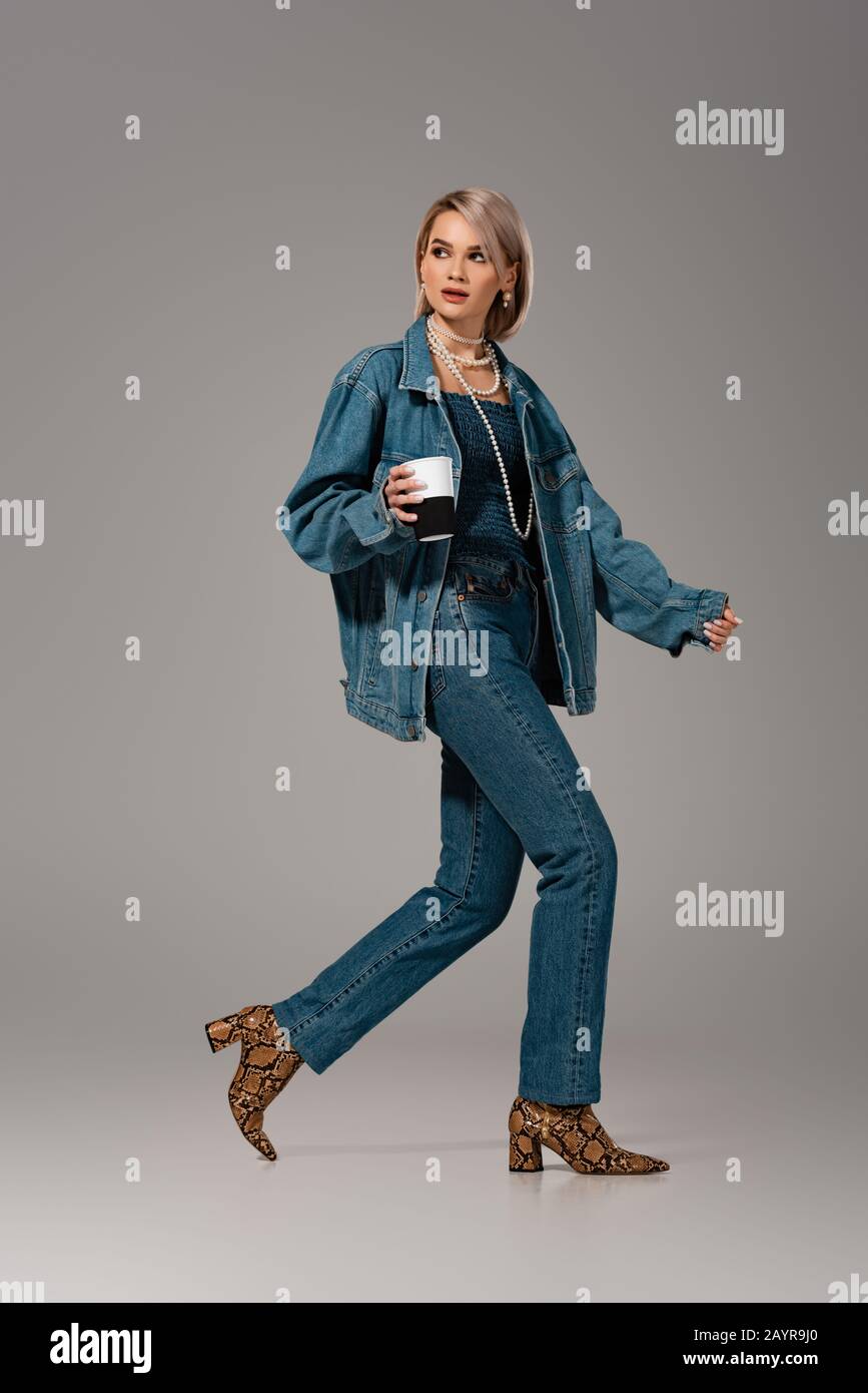 attractive woman in denim jacket and jeans holding insulated mug on ...