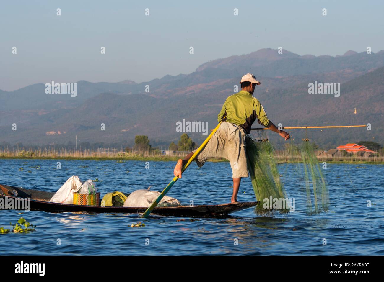 A leg-rowing fisherman in his boat is setting fishing net on Inle Lake ...
